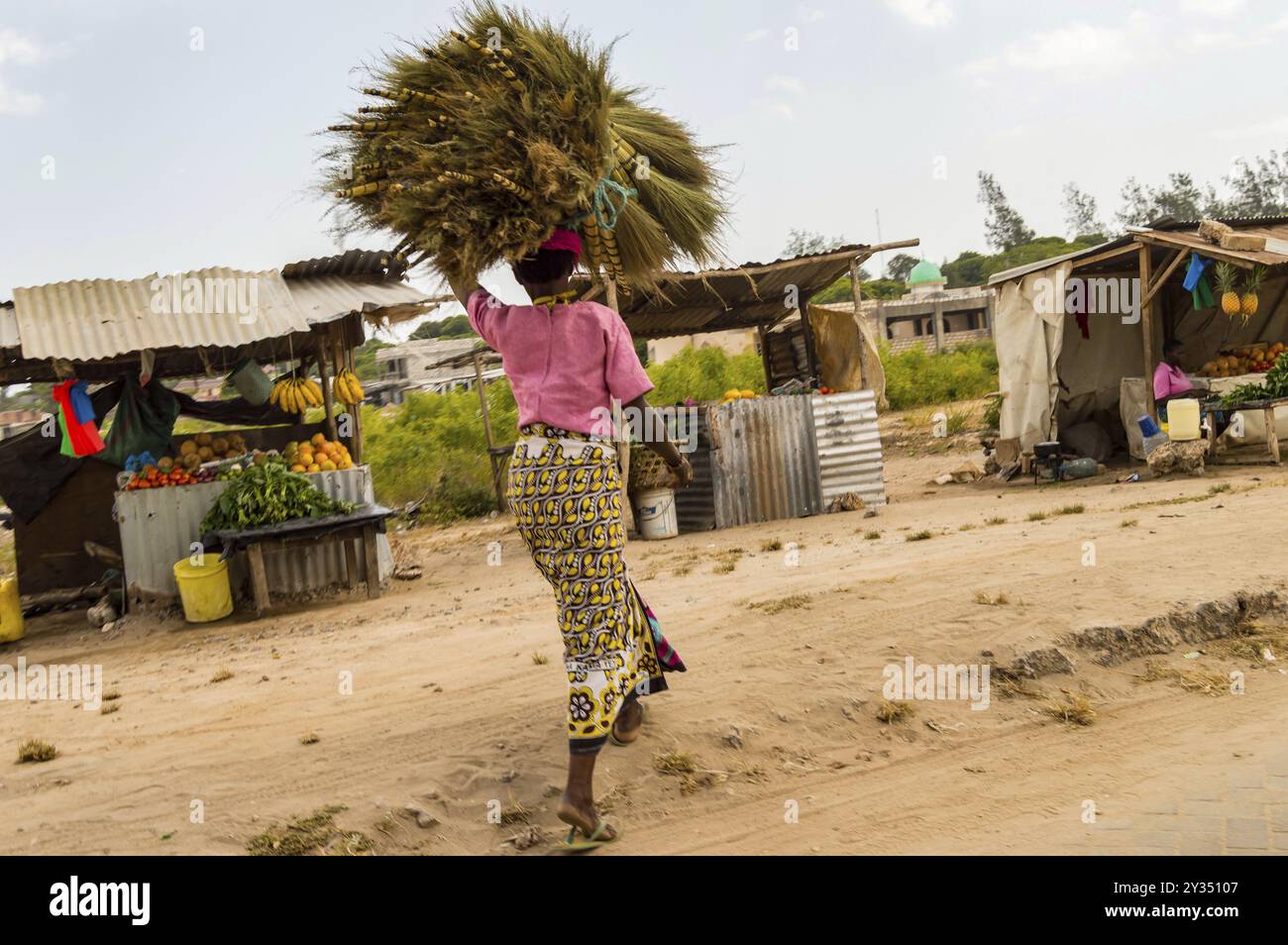 African woman carrying a bundle on her head in a small market near ...