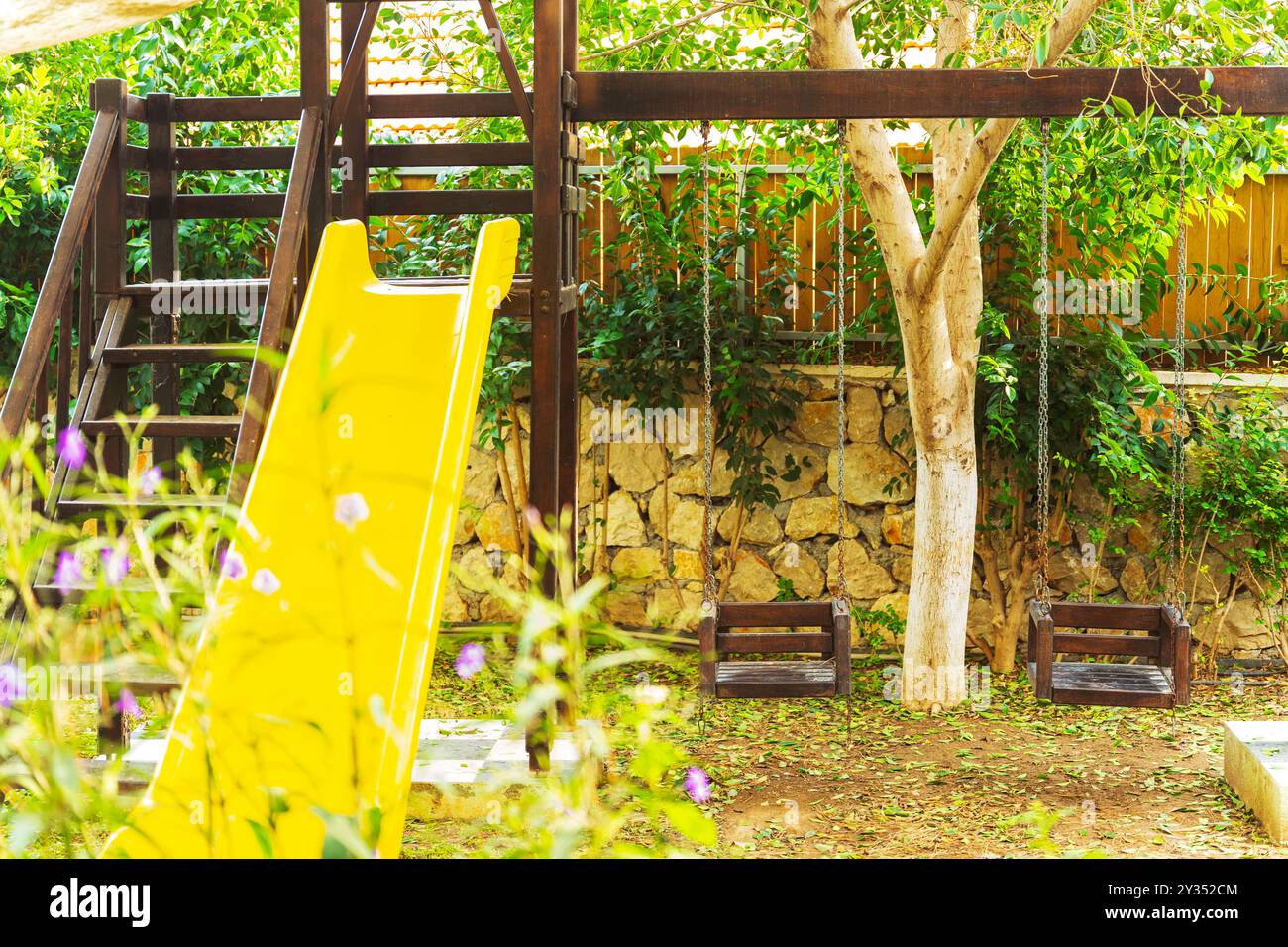 A wooden playground with a bright yellow slide and swings for kids ...