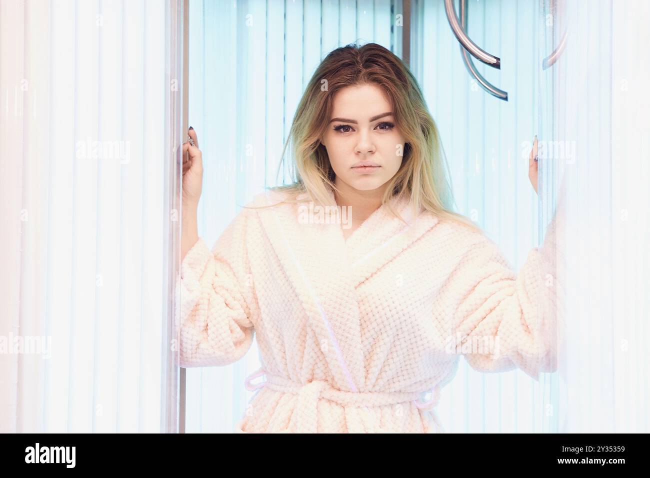 Woman in bathrobe standing in tanning booth with bright lights and calm ...