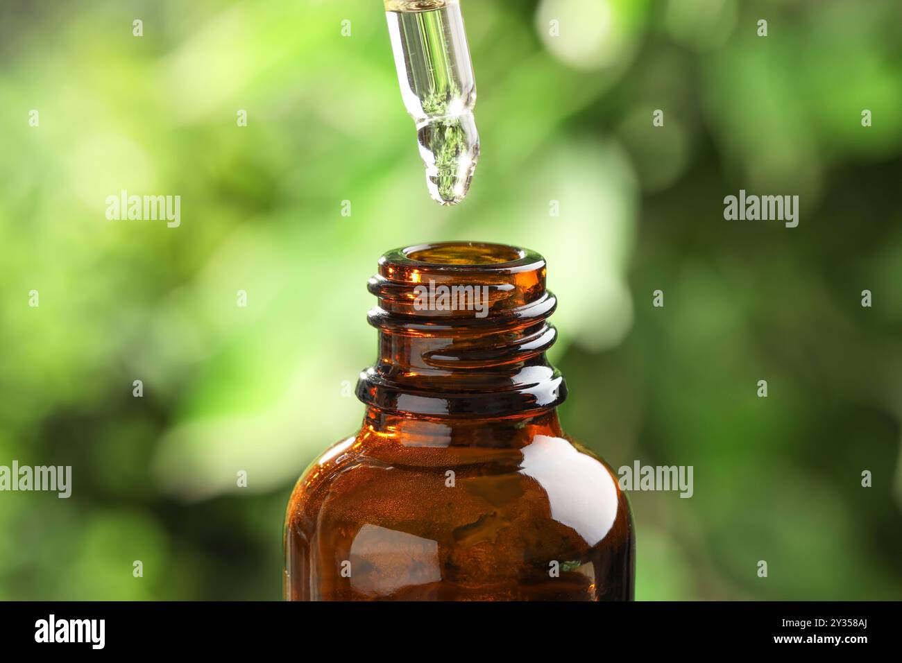 Essential oil dripping from pipette into bottle against blurred green ...