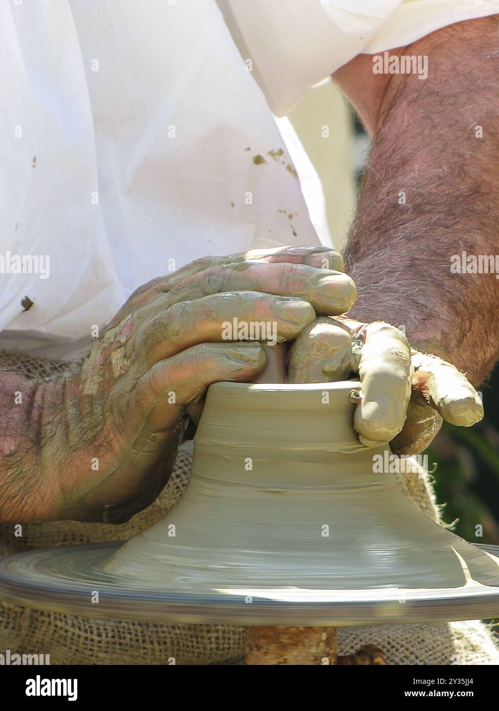 A skilled potter sits in an open-air workshop, spinning a clay wheel ...