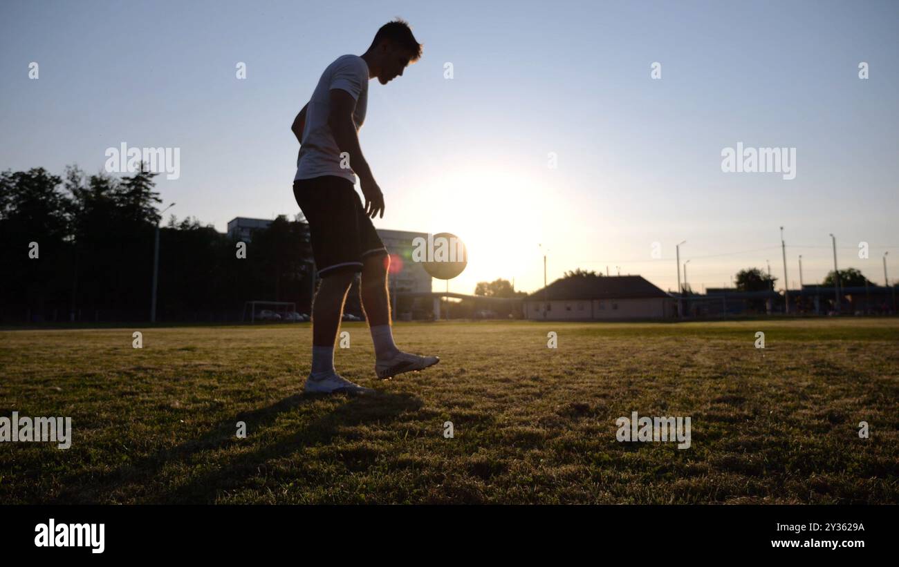 Professional footballer juggling soccer ball on stadium at sunset ...