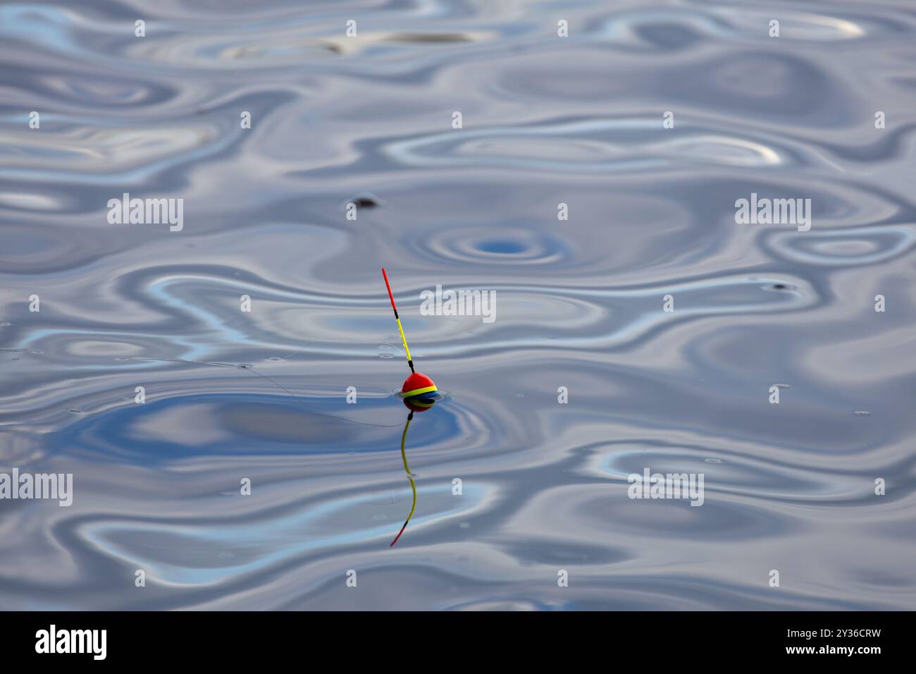 A colorful fishing bobber floats on the surface of a calm water body ...