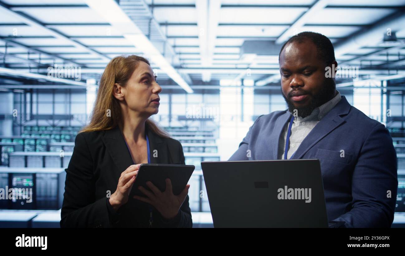 Teamworking technicians managing data center with advanced technology using devices. Coworkers ...
