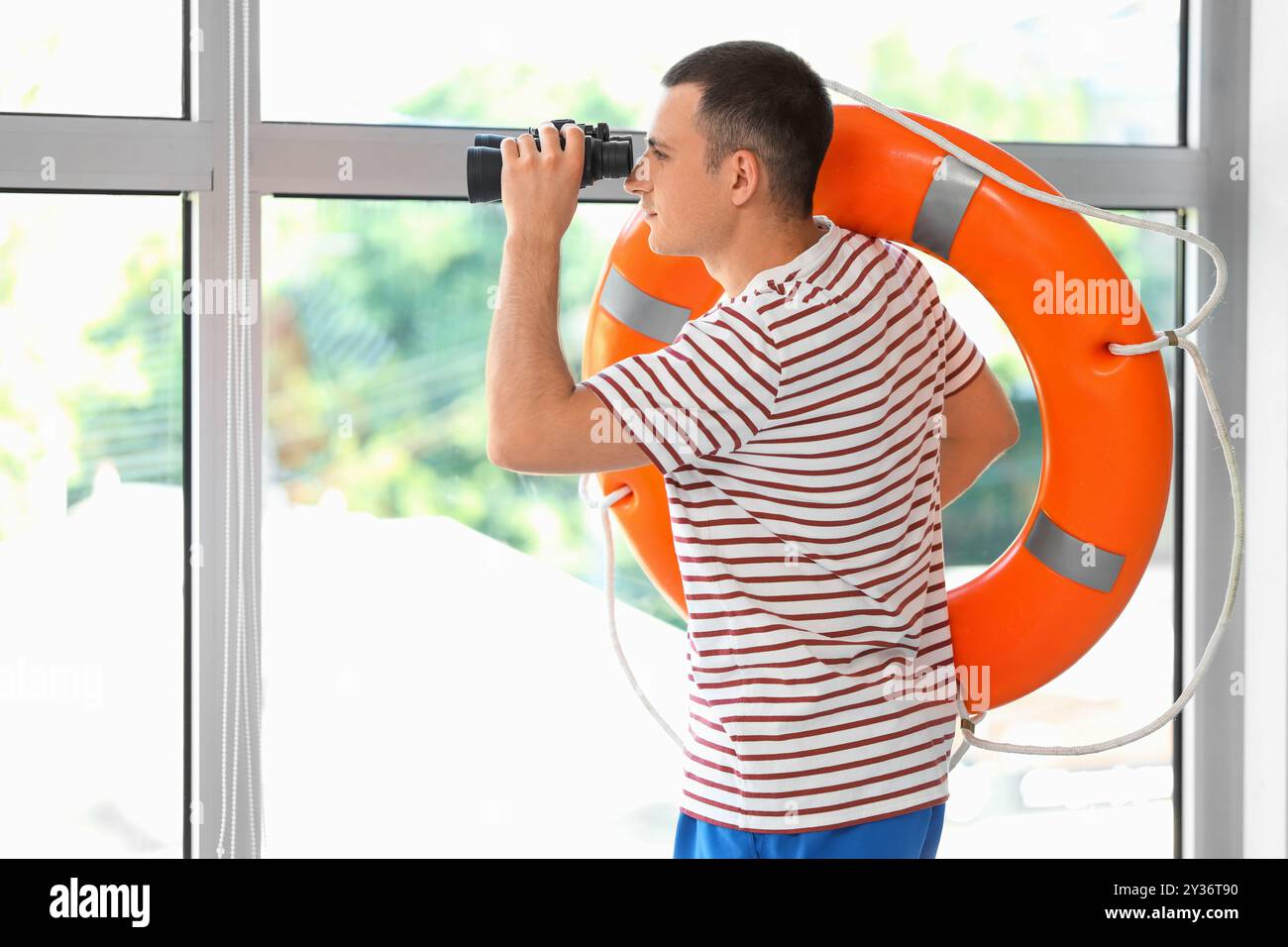 Male lifeguard with ring buoy and binoculars near window in pool Stock ...