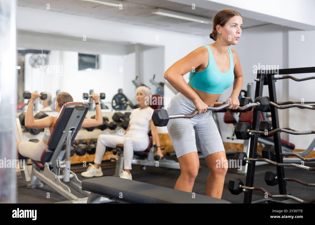 Slender girl trains muscles of arms and back using barbell and ...