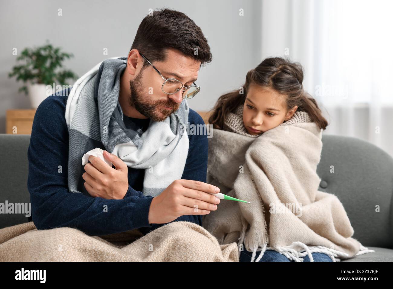 Cold symptom. Father with his daughter suffering from fever on sofa at ...