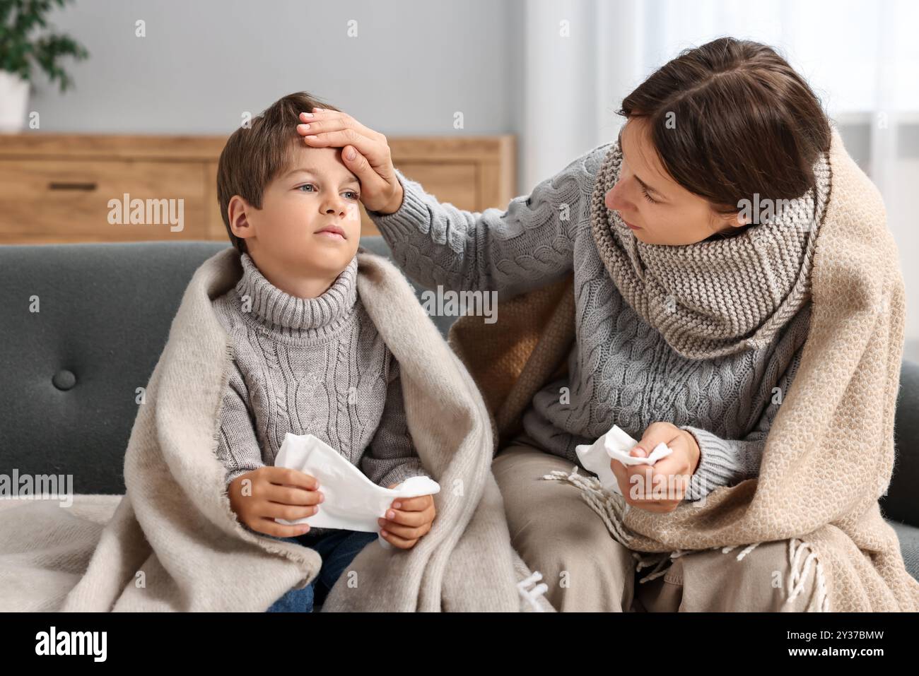 Cold symptom. Woman with her son suffering from fever on sofa at home ...