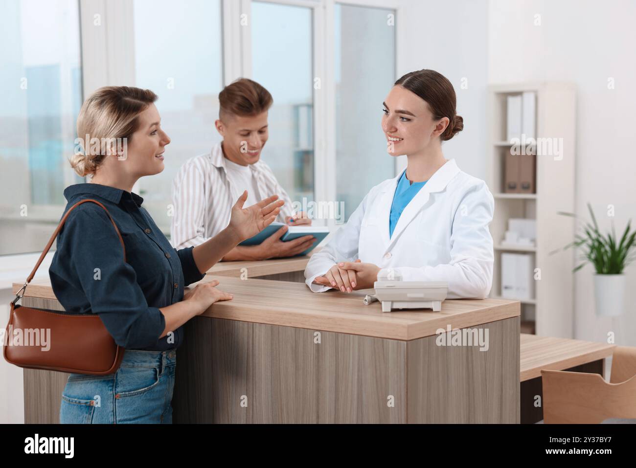 Professional receptionist working with patients at wooden desk in ...