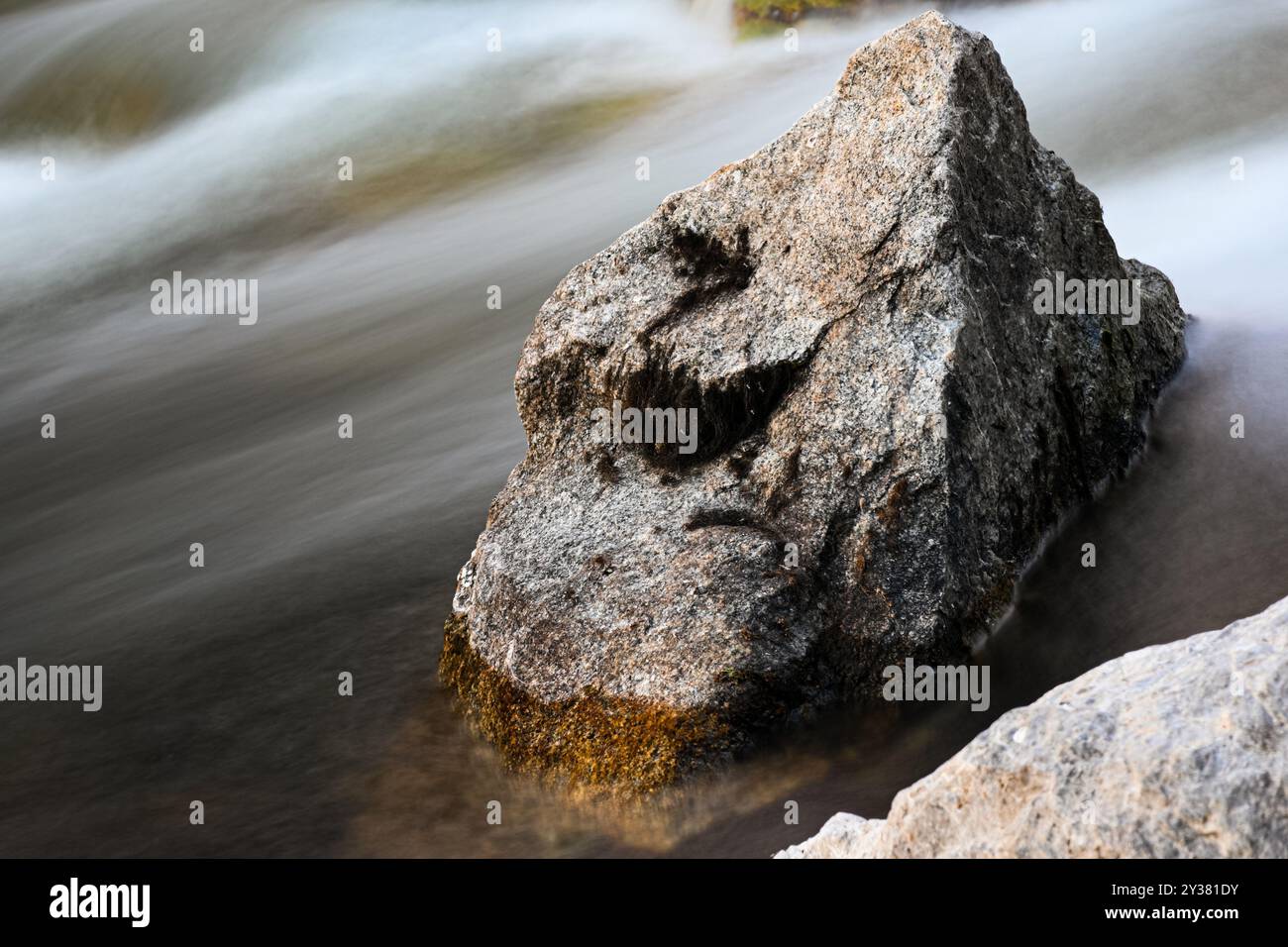Water flows quickly around rocks in a creek, creating a smooth, silky ...