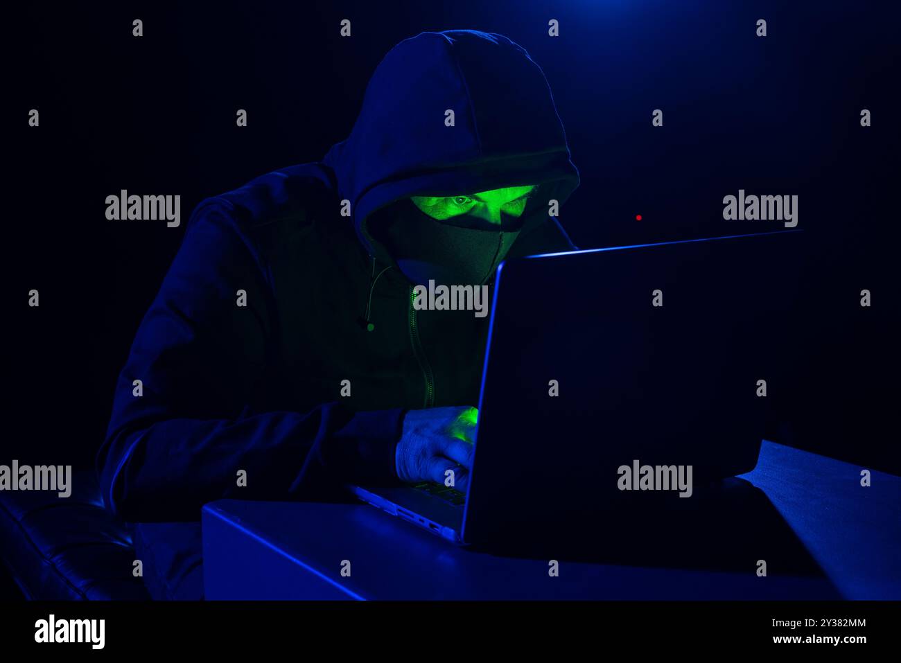 Cyber hacker in hood behind laptop in dark room, digital cyber security concept, computer ...