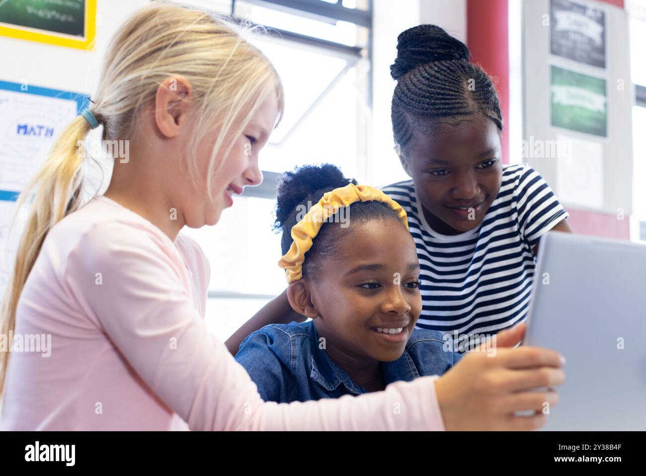 In school, three multiracial girls using tablet together, smiling and ...