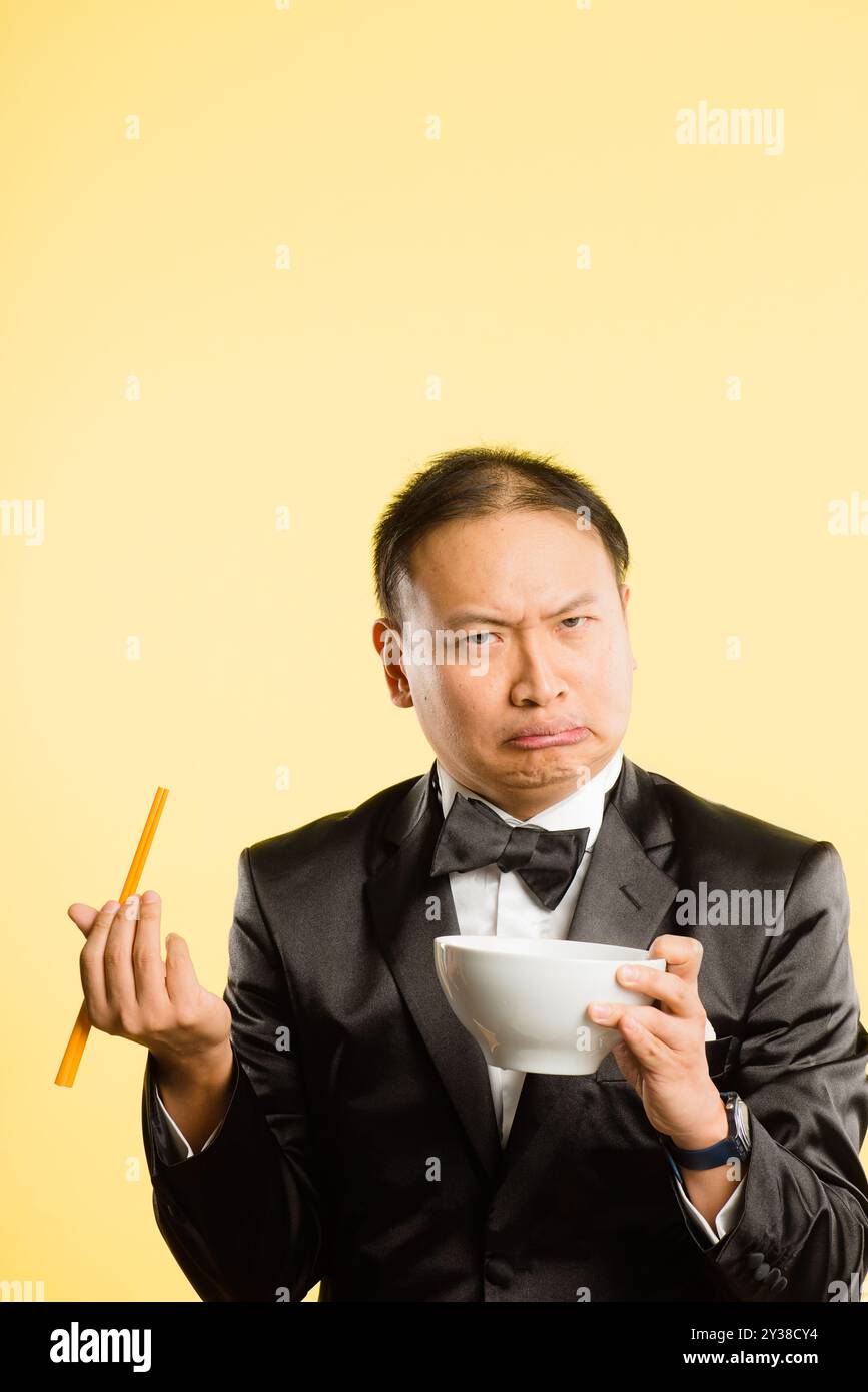 Man, chopsticks and portrait in studio with funny face, tuxedo and ...