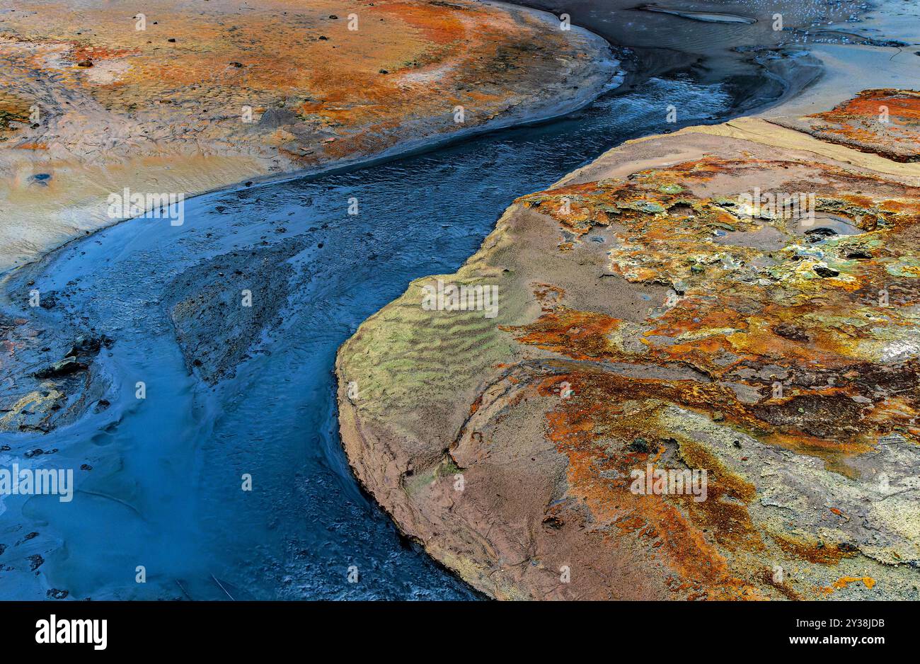 a river of dark water flows from a hot spring. the surrounding soil is ...