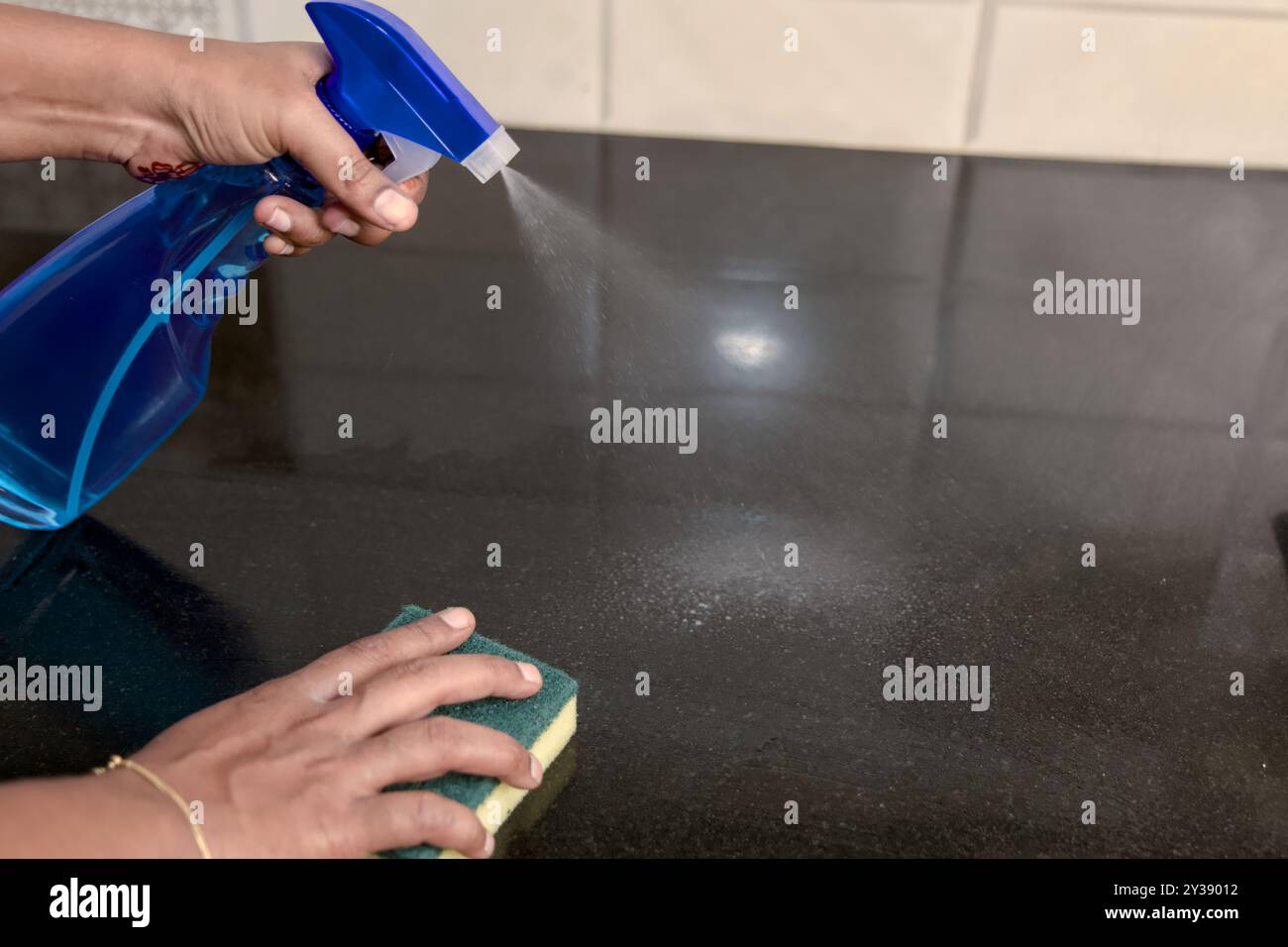 Hands using spray bottle and sponge to clean a modern black kitchen ...