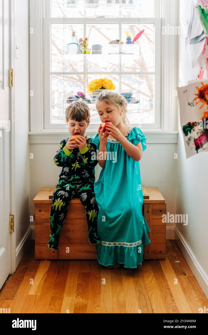 Two children sitting together by a window, eating apples Stock Photo ...