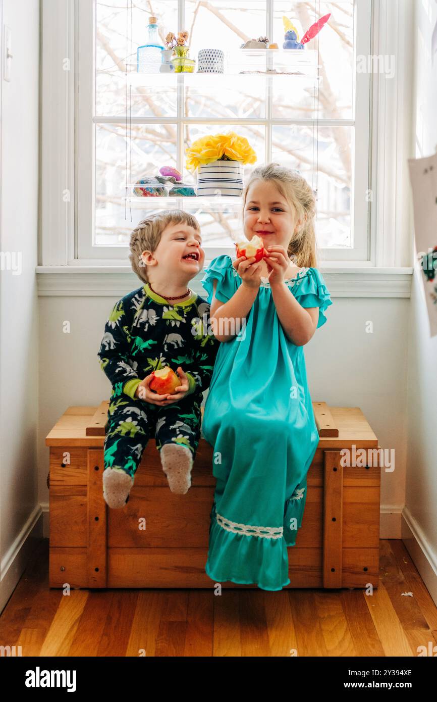 Two children sitting together by a window, happily eating apples Stock ...