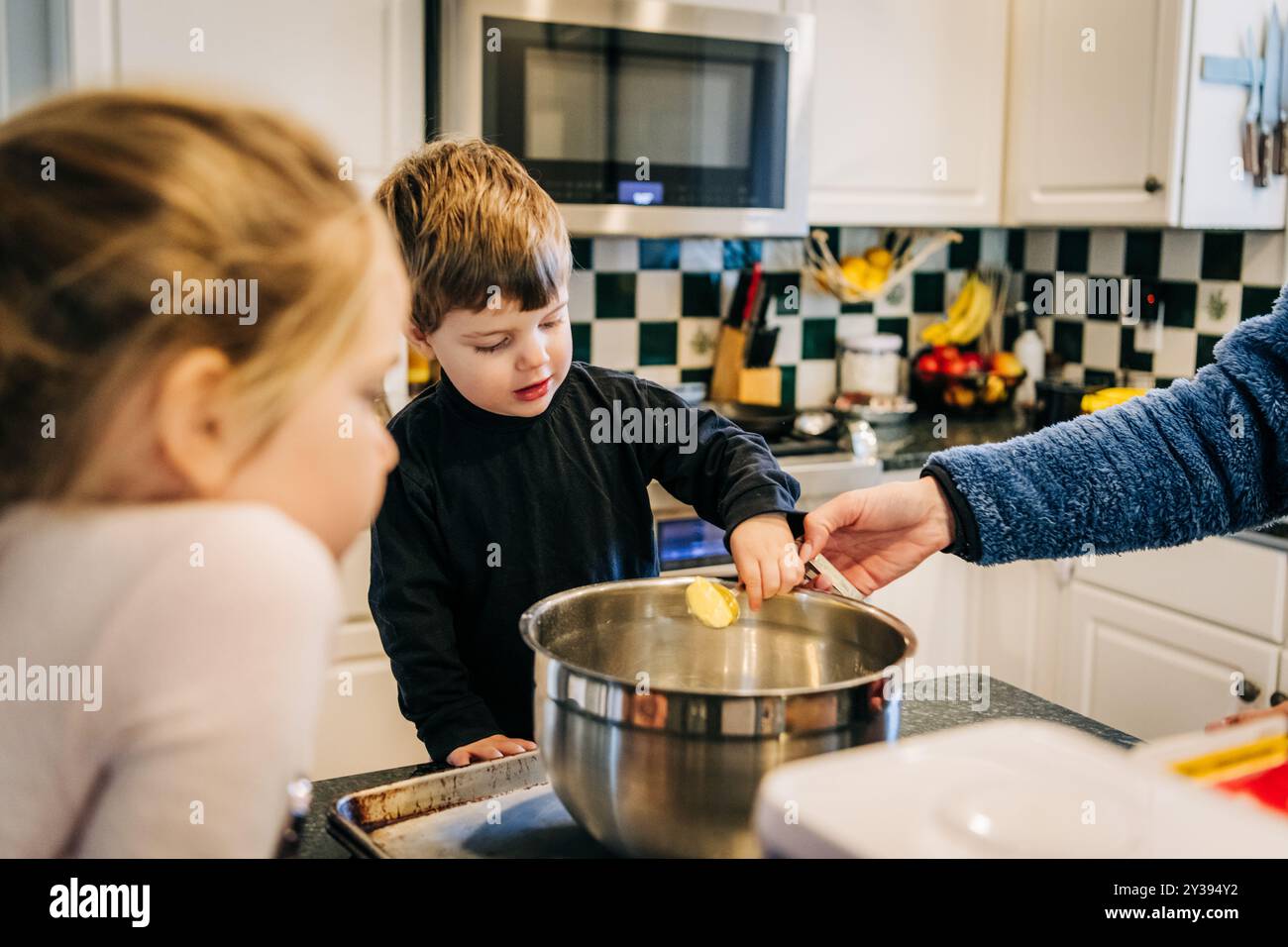 Two children baking in the kitchen, adding butter to a mixing bowl ...