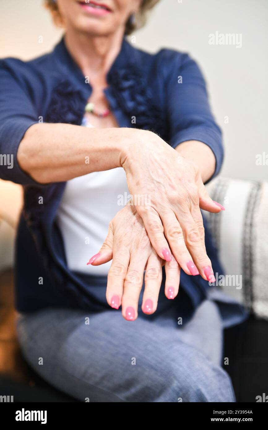 Smiling woman poses for a portrait, sitting with hands folded on Stock ...