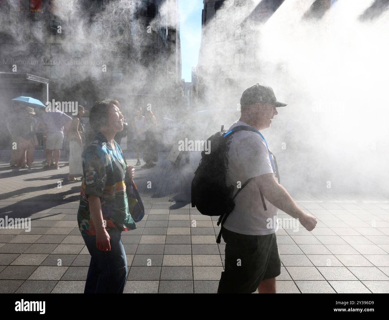 People walk under a mist-generation device in the heat in Tokyo, Japan ...