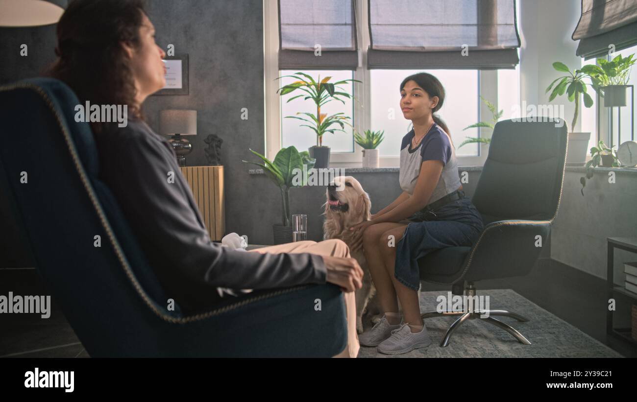 African American teenage girl sits in chair, listens to therapist, pets ...