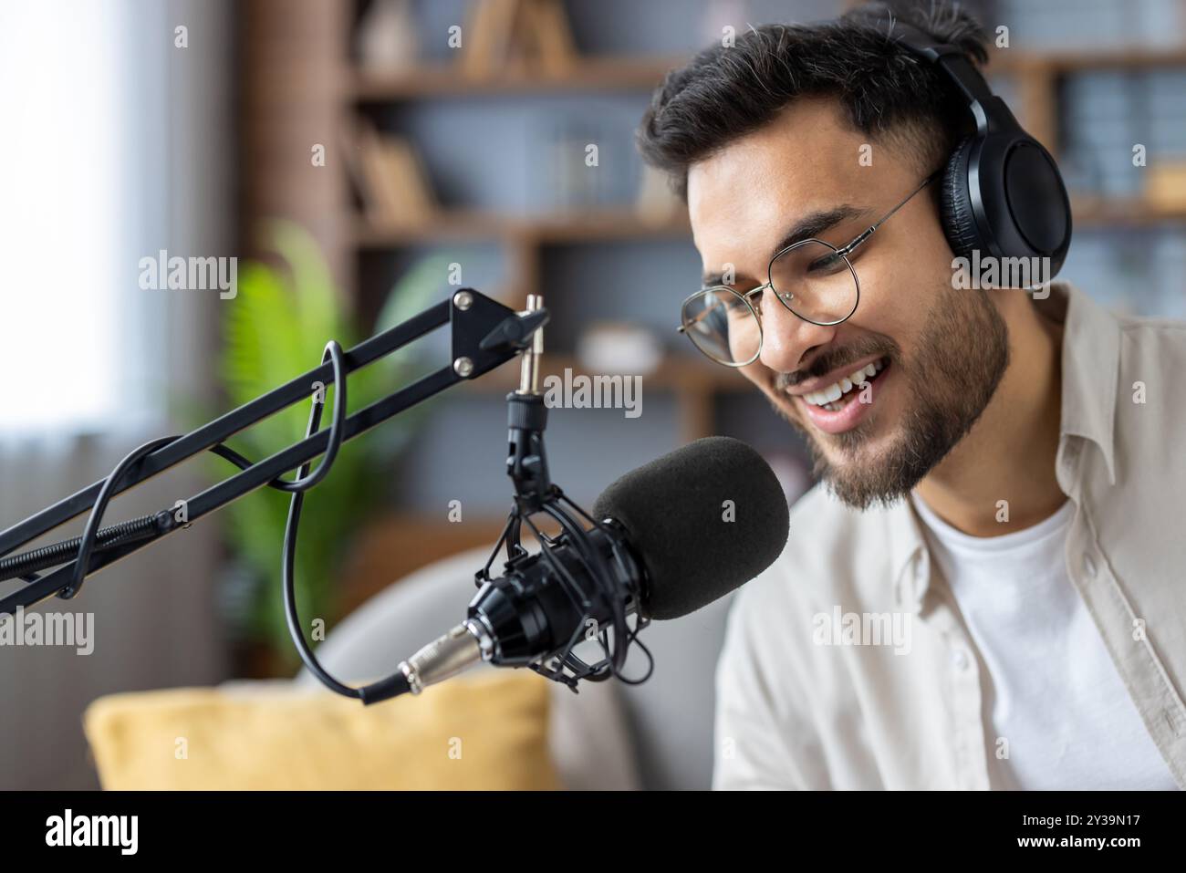 Hispanic man wearing headphones and smiling while recording podcast ...