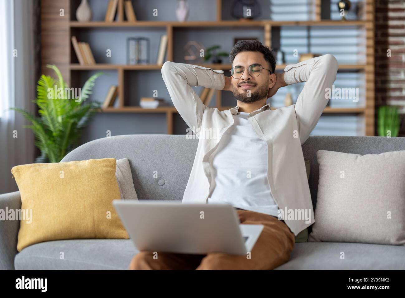 Young relaxed Indian man sitting on sofa at home, holding laptop on lap ...