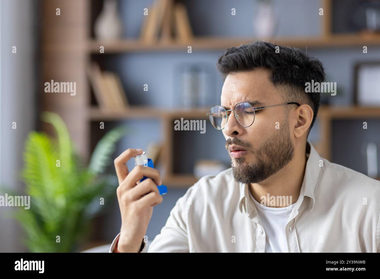 Close-up photo of a young Indian man at home, holding an inhaler and ...