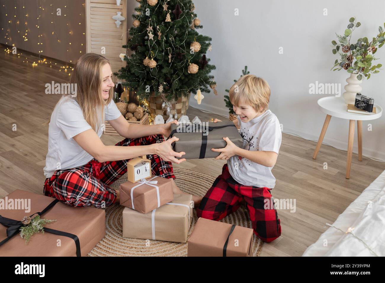 Mom and son sit on floor in front of New Year tree next to many gift ...