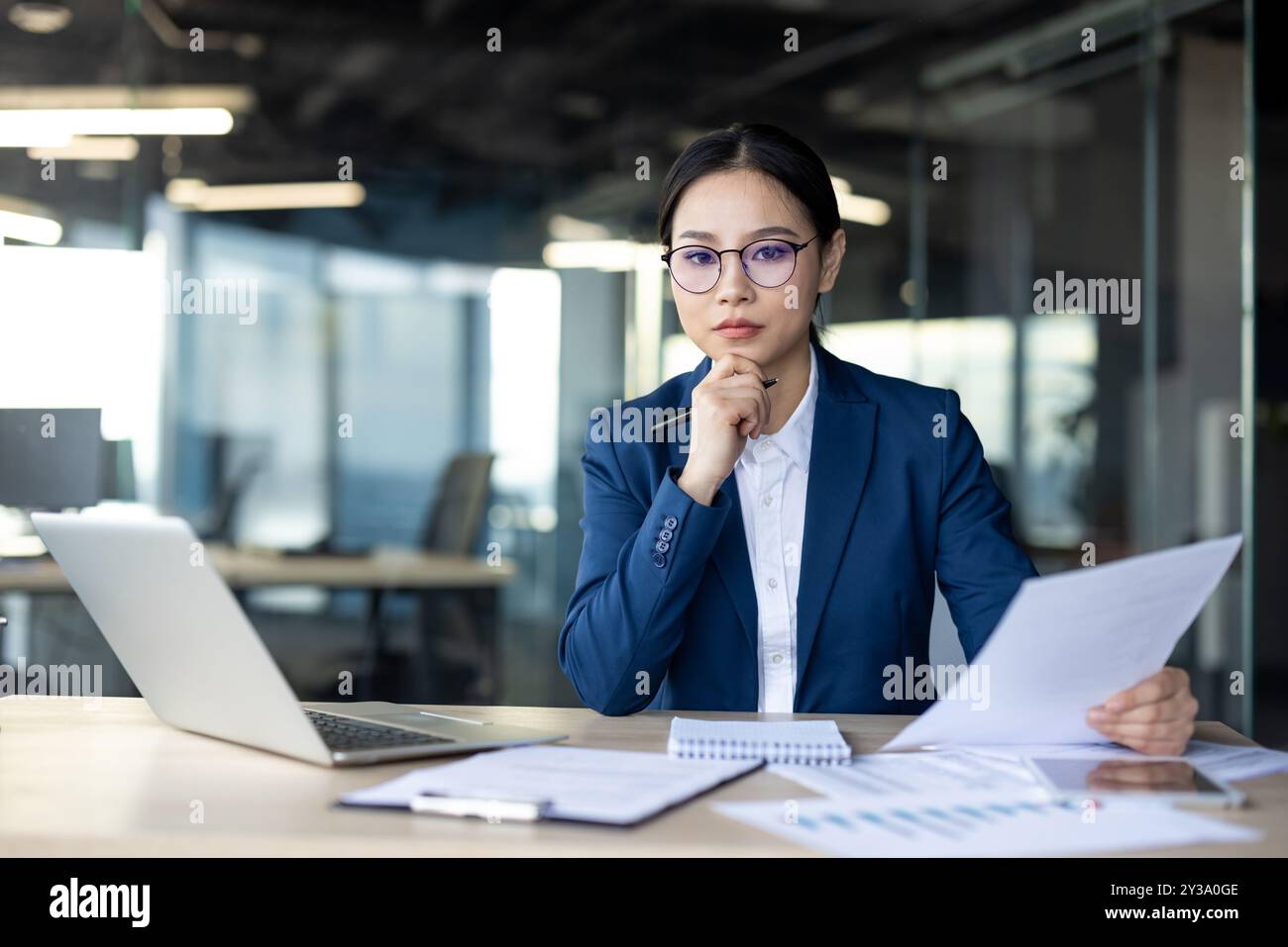 Asian business woman reviewing documents at office desk with serious ...