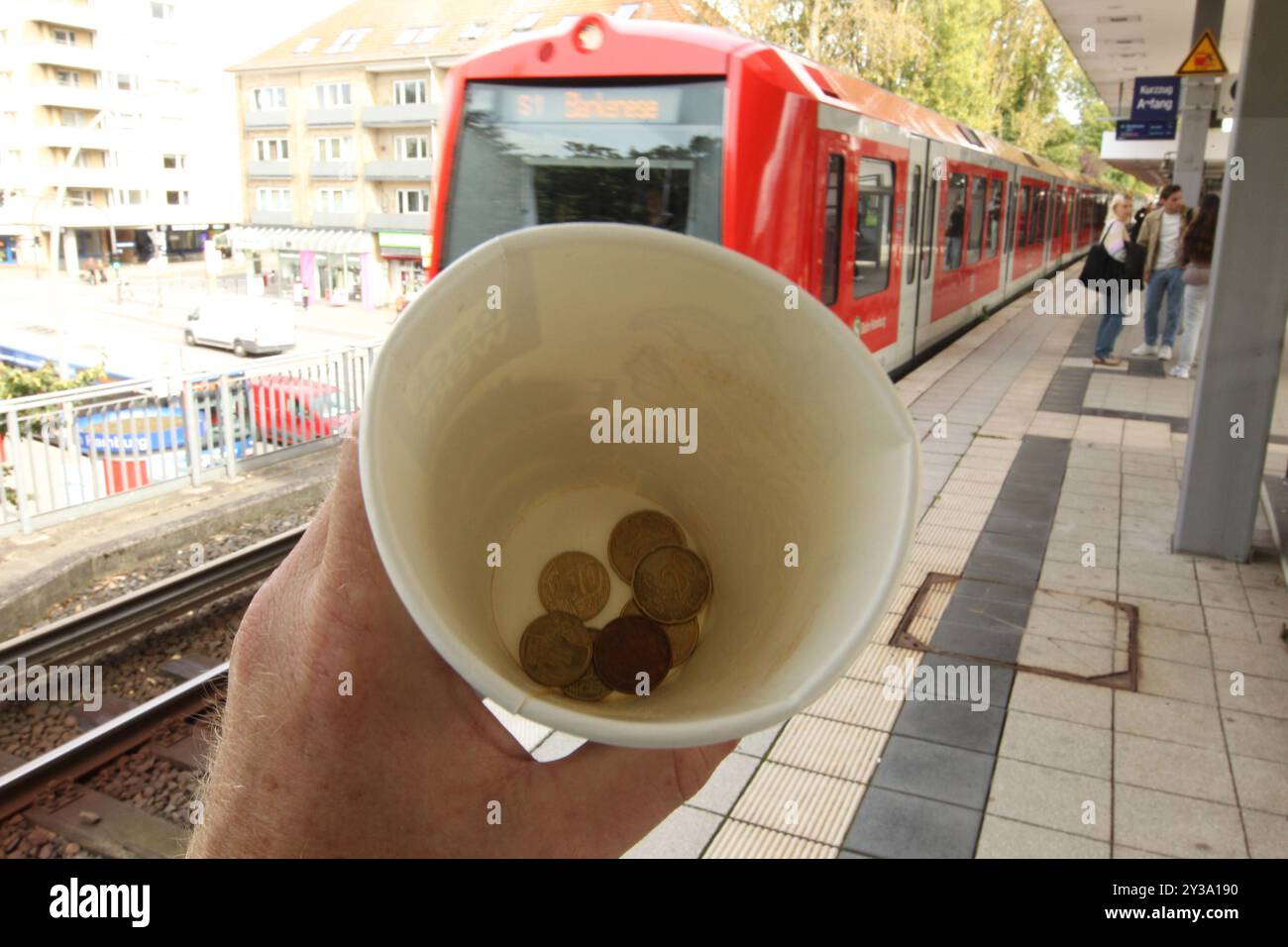 Ein Mann hält auf einem Bahnsteig einen Becher mit Kleingeld in der ...