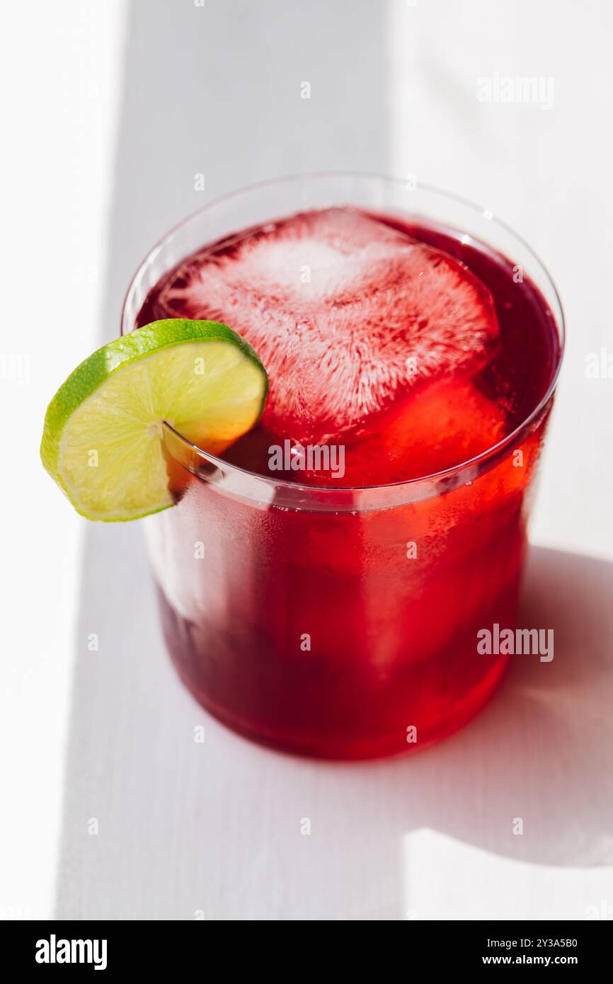 hibiscus tea drink with ice in rocks glass, lime wheel garnish, white ...