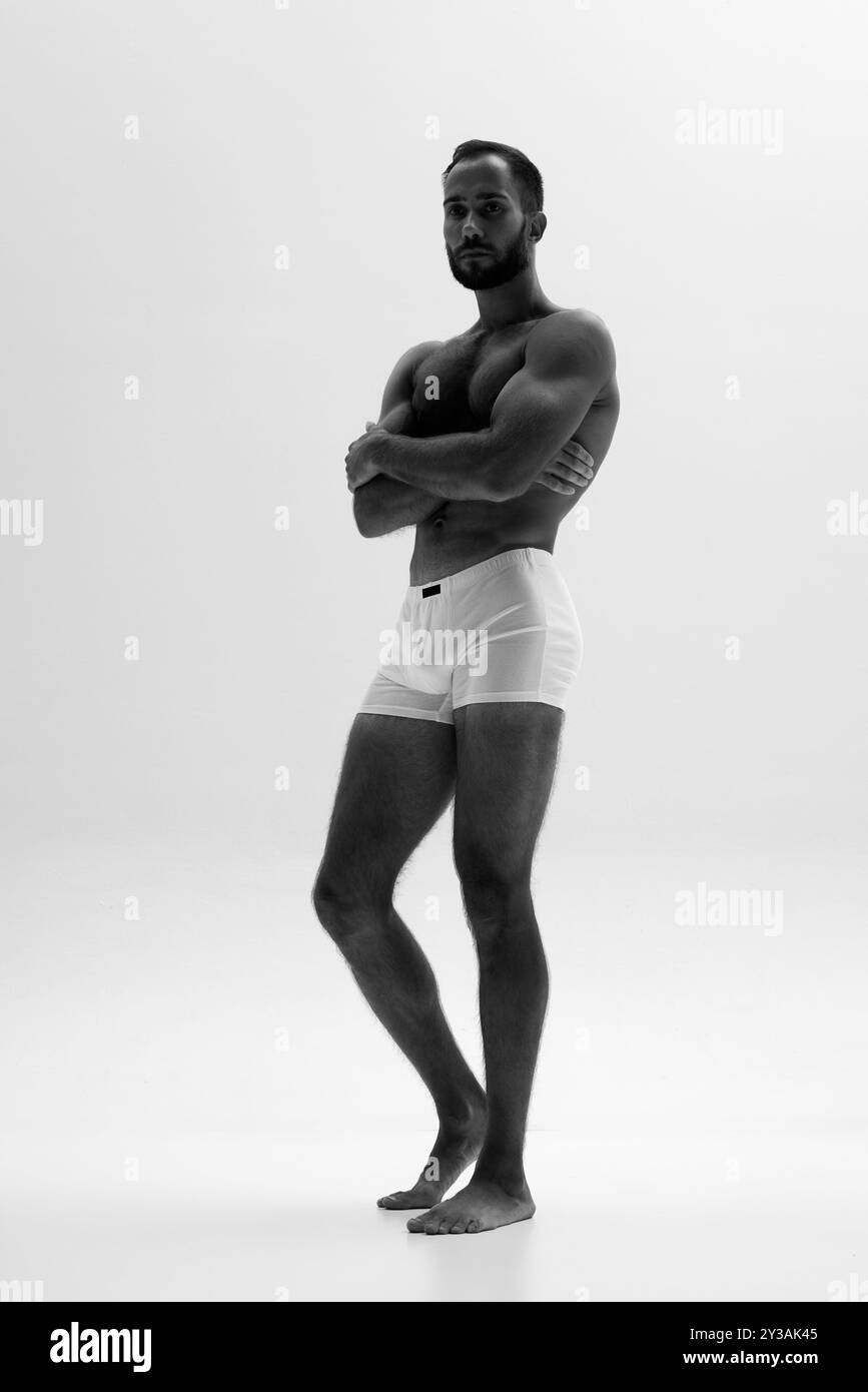 Muscular man stands confidently in white boxer briefs, showcasing his ...