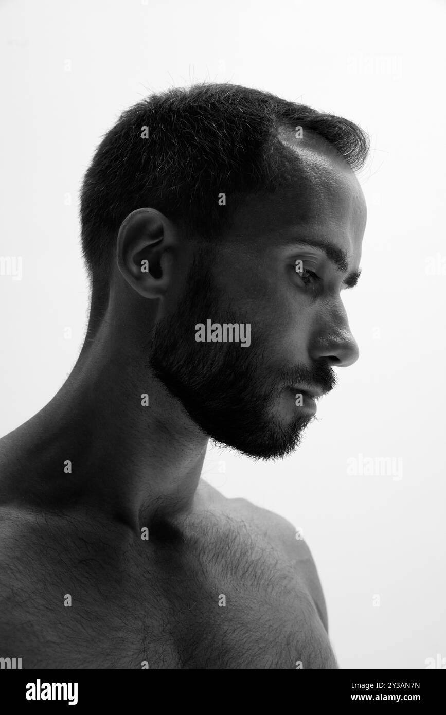 Bearded man stands in profile with thoughtful expression against white ...