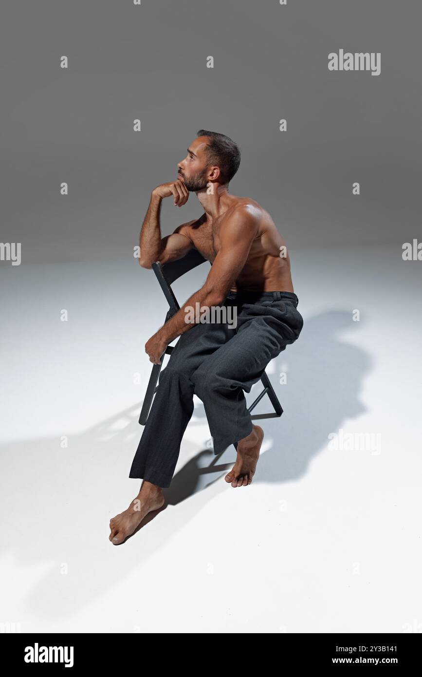 Thoughtful man, sitting on chair with one hand resting on his chin ...