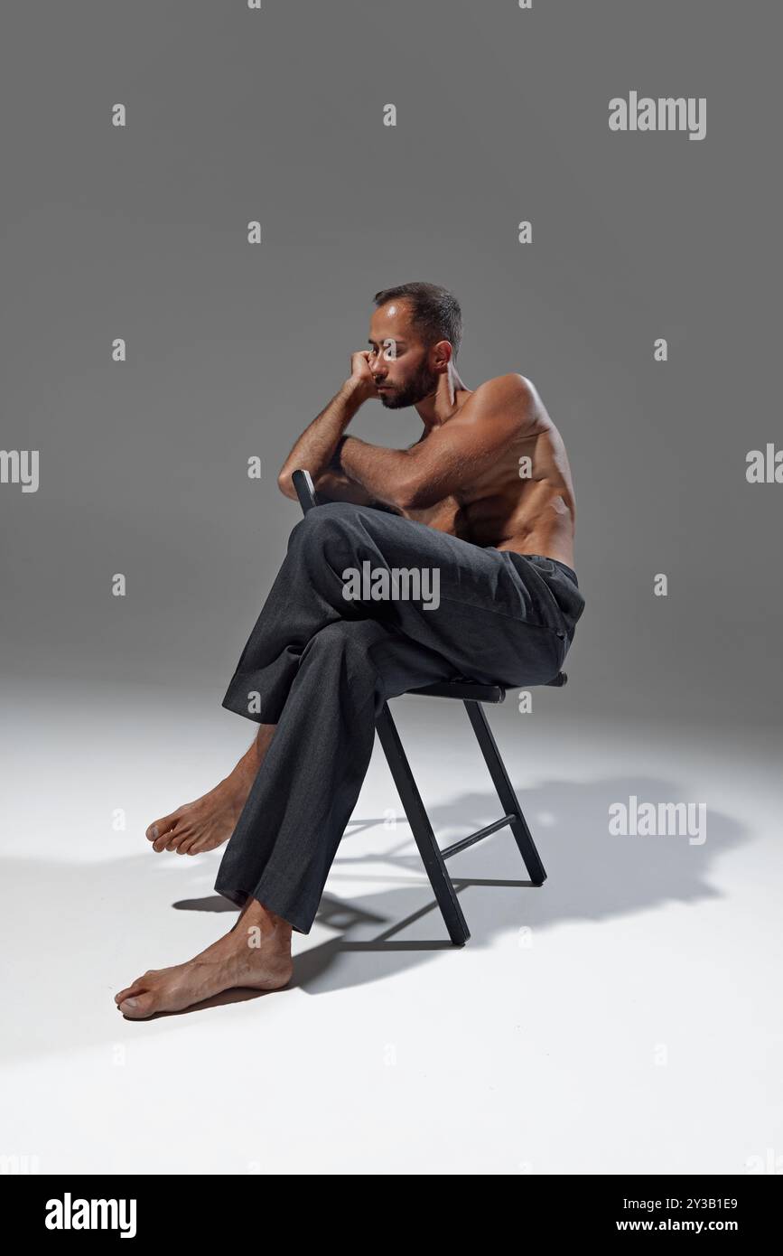 Thoughtful man, sitting on chair with one hand resting on his chin ...