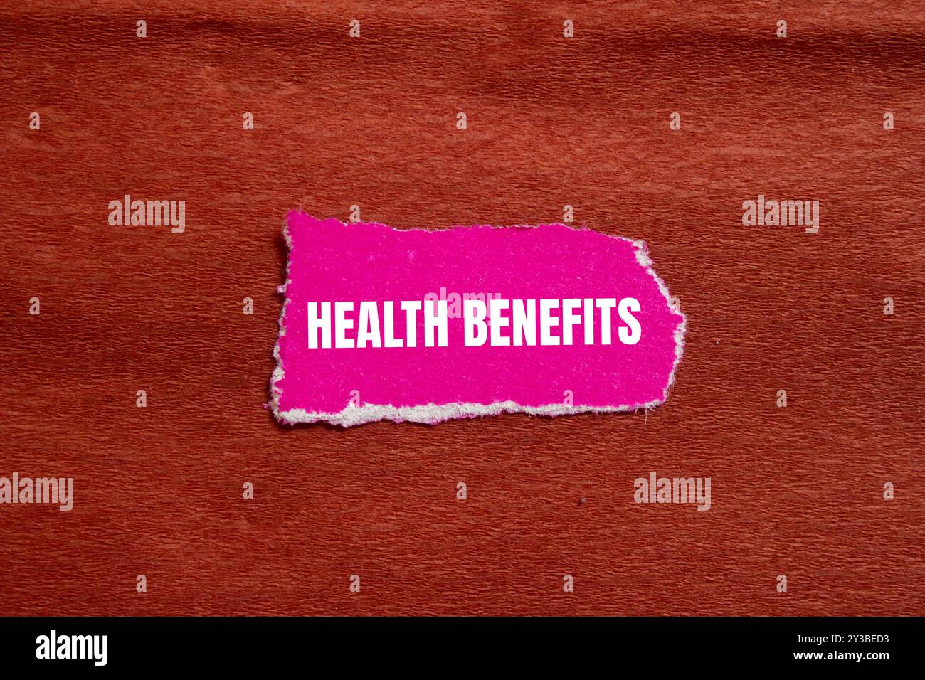 Health benefits message written on ripped torn pink paper piece with brown background ...