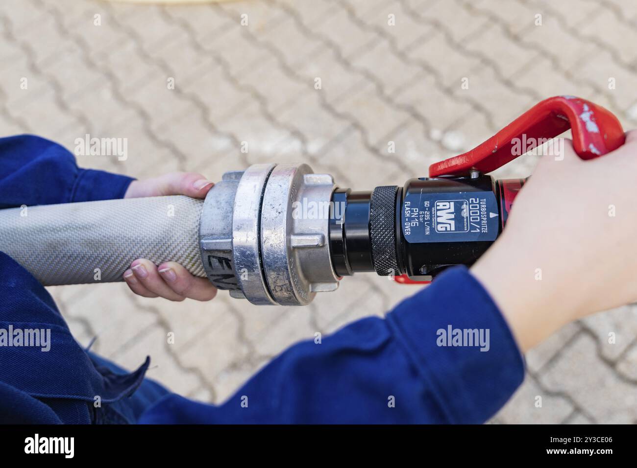 Child holding a fire hose with a connected metal coupling, fire brigade ...