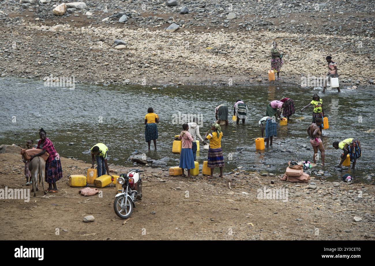 Women with plastic jerrycans fetching water and washing their bodies at ...