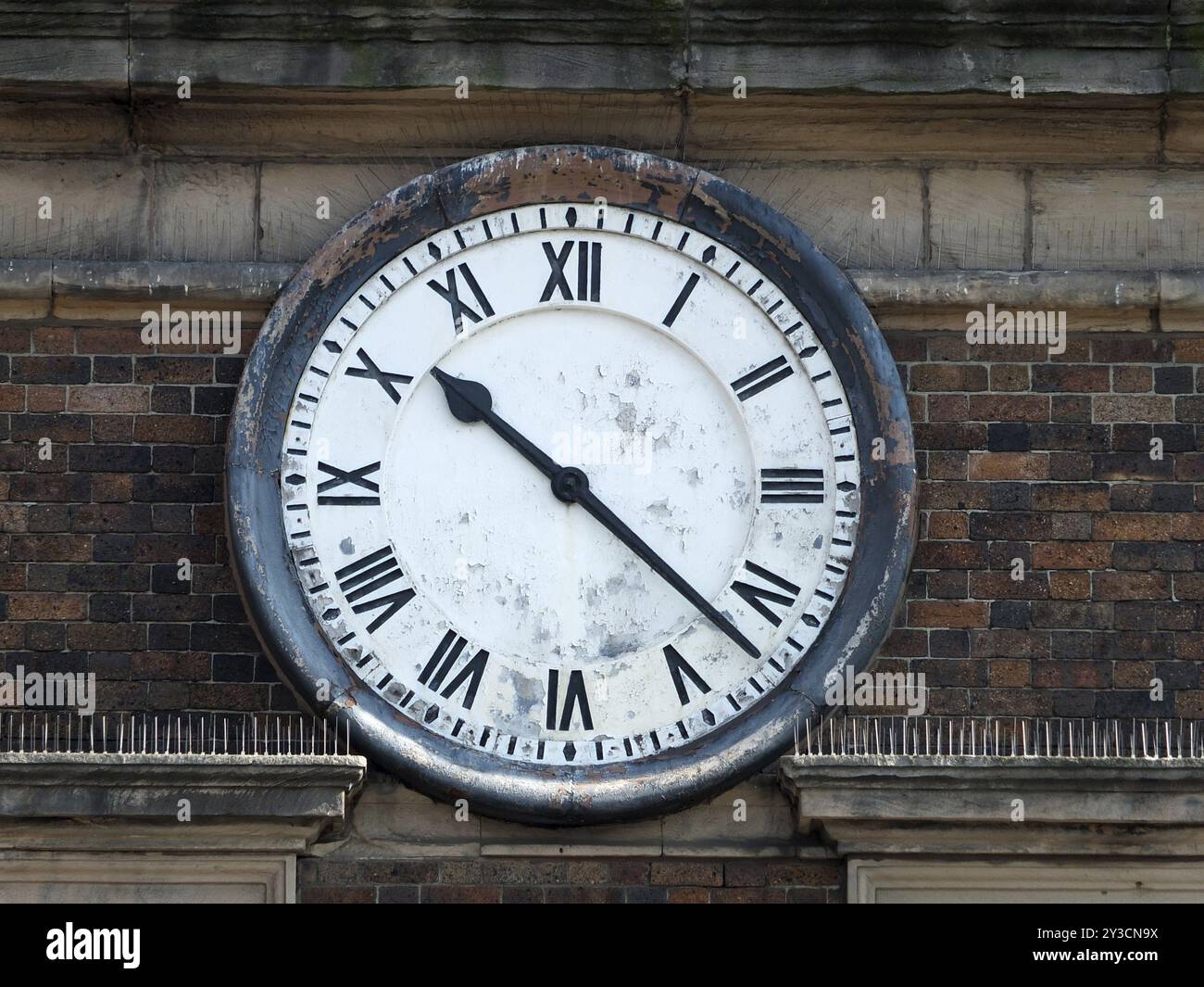 Old round clock on the brick wall of a building with roman numerals and ...
