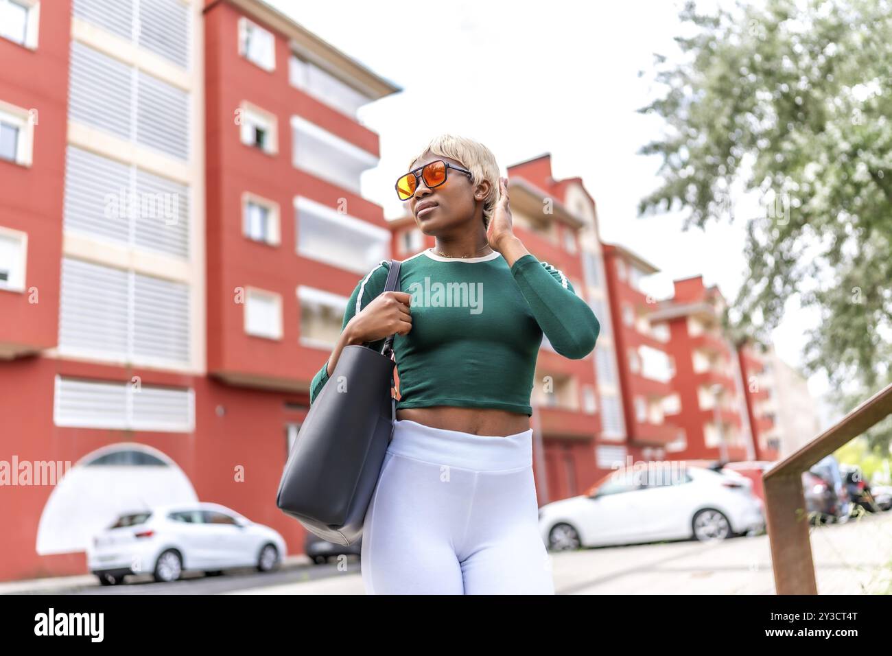 Urban african woman with blonde short hair in casual clothes and sunglasses walking alone in the ...
