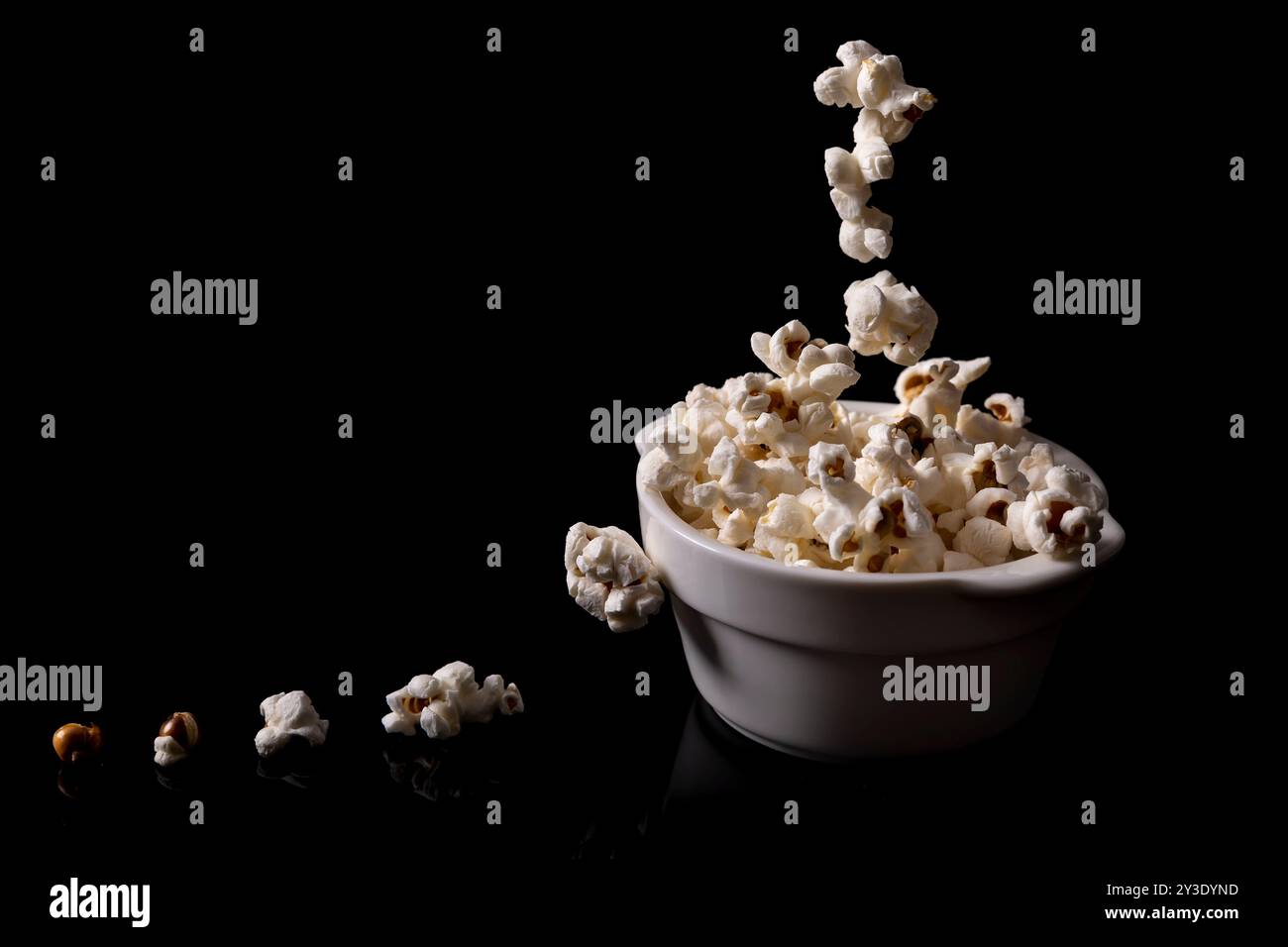 Popcorn popping in the air above a white bowl, on a shiny black ...