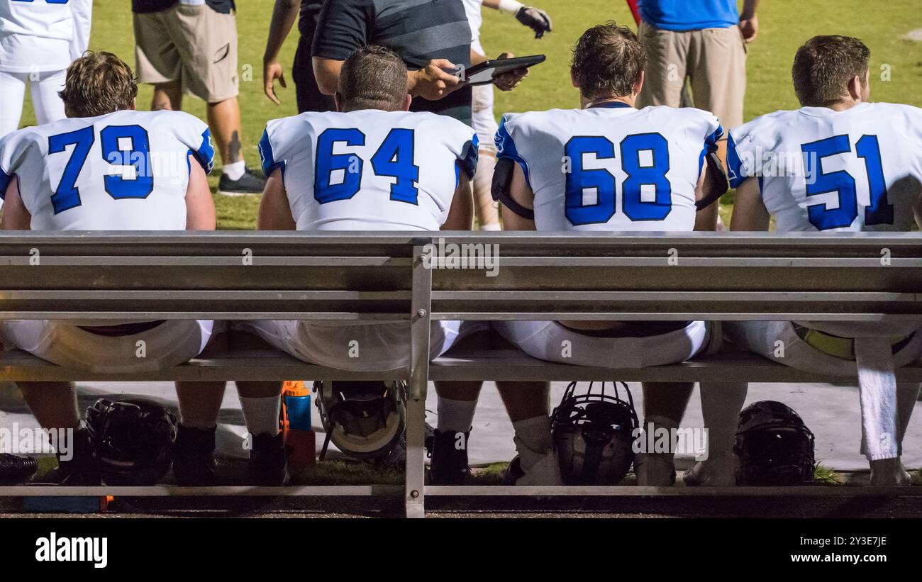 Four large American football linemen sit on the bench as they receive ...