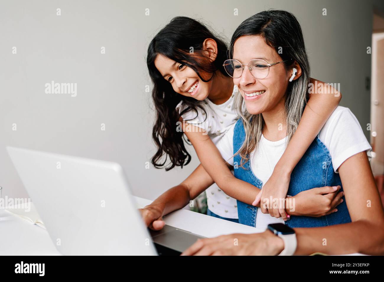 Black working mother using computer laptop at home office. Happy daughter hugging mom. Family ...