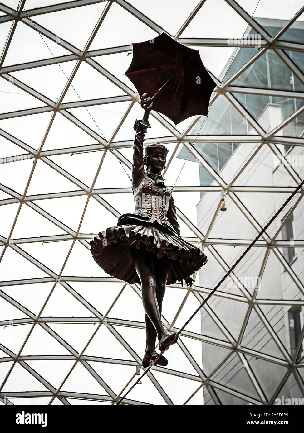 the statue of a woman with an umbrella walking on a suspended wire ...
