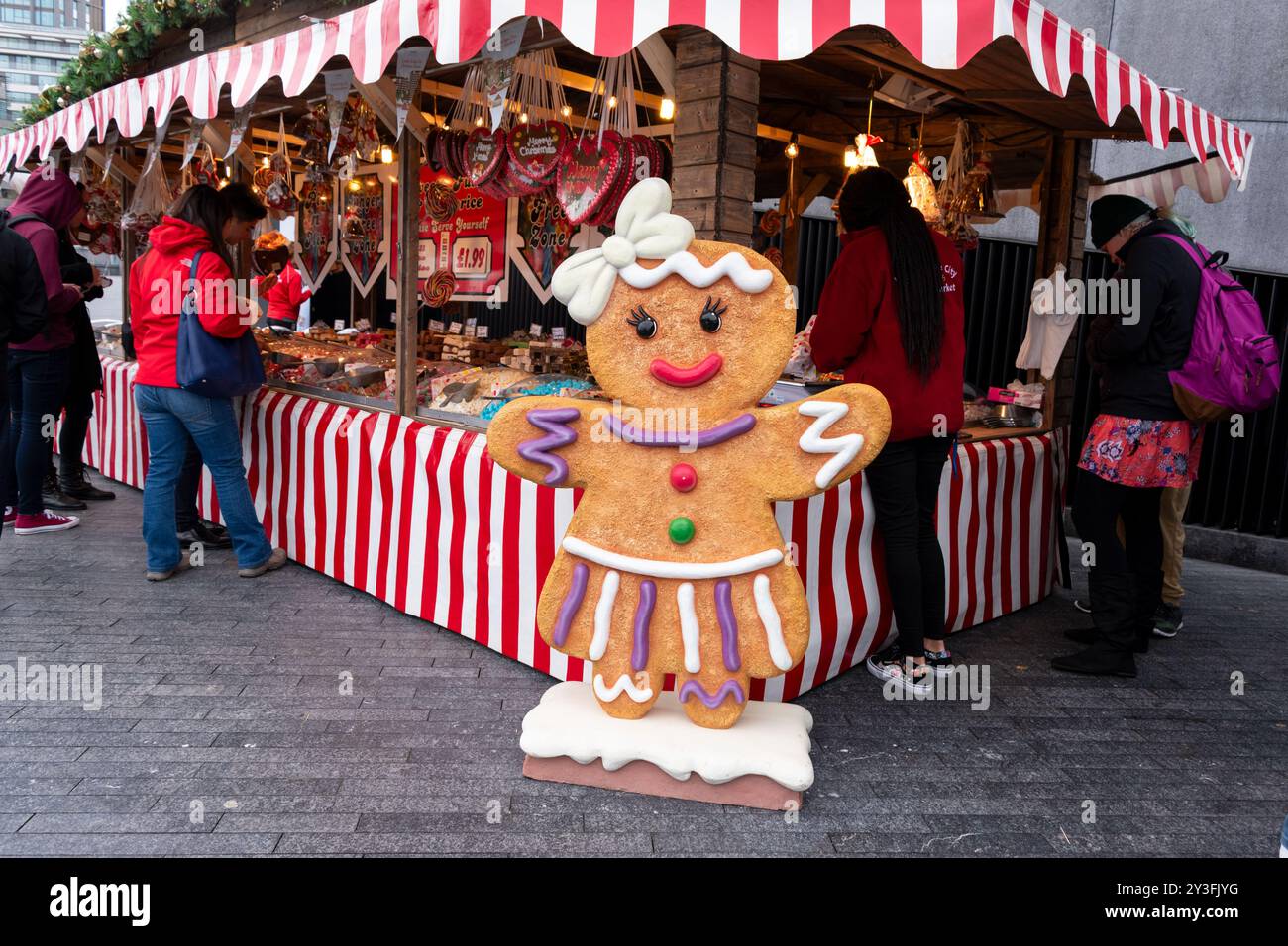 A gingerbread woman in front of a Christmas market stall, crowded with ...
