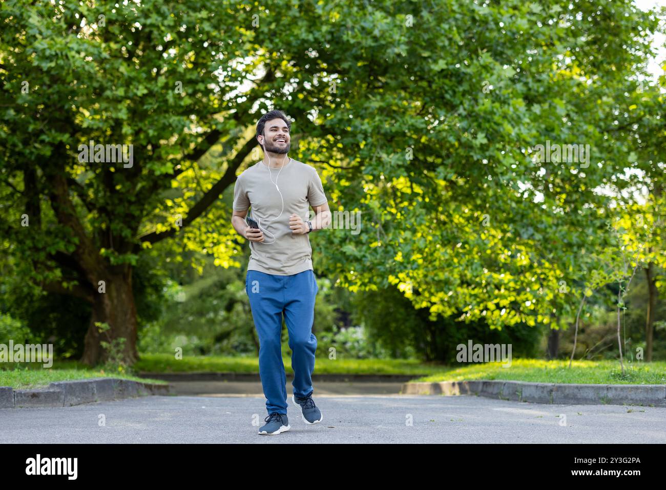 Young man jogging outdoors surrounded by green trees, listening to ...