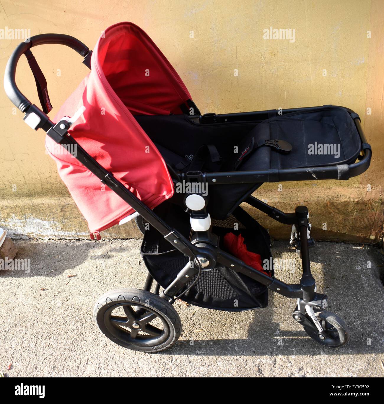 A fashionable red-black empty baby carriage in a garden in front of the ...