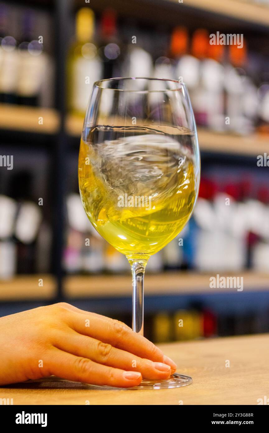 A glass of white wine with a hand on the glass, swirling the wine ...
