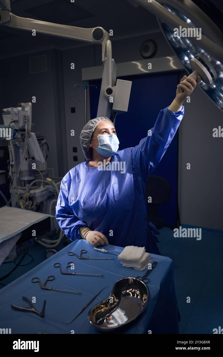Female surgeon assistant reaches up to adjust overhead surgical light ...